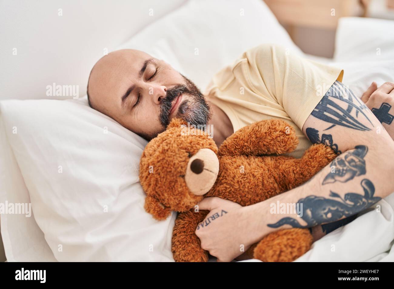 Young Bald Man Hugging Teddy Bear Lying On Bed Sleeping At Bedroom