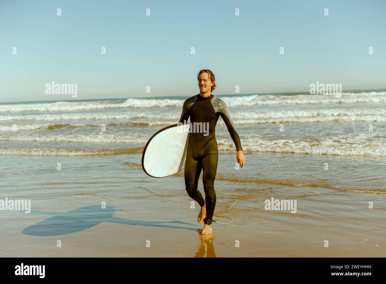 Happy handsome male surfer in wetsuit with his surfboard entering out ...