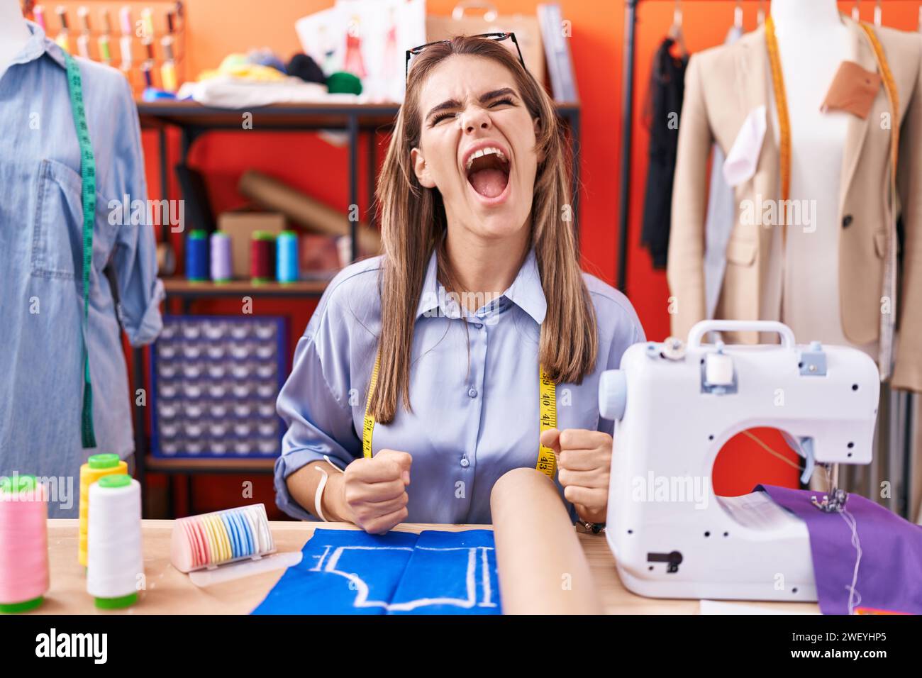 Hispanic young woman dressmaker designer at atelier room angry and mad screaming frustrated and ...