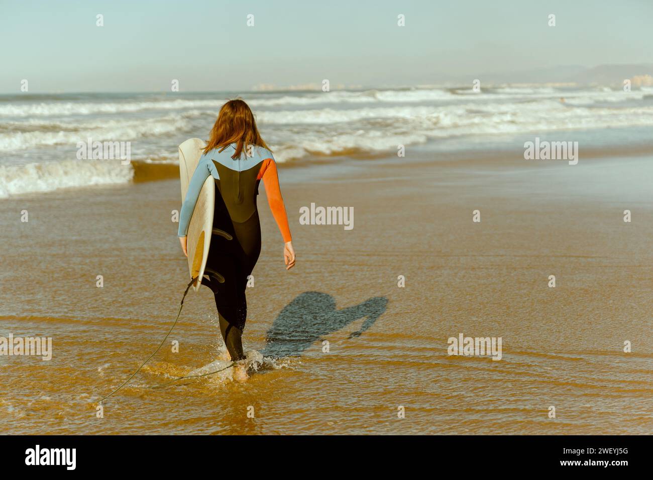 Back view of female surfer in wetsuit with his surfboard entering the ...
