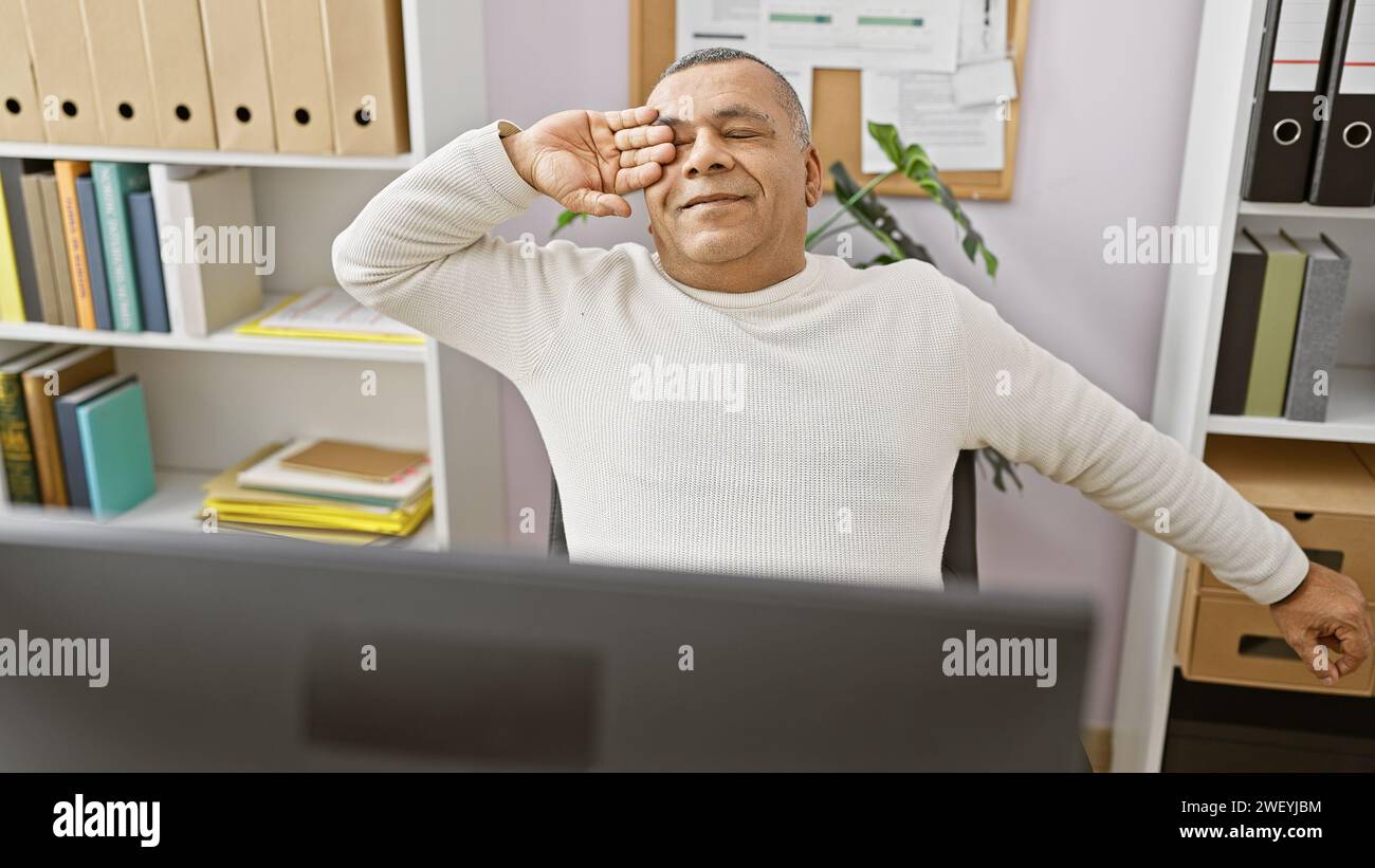 Tired middle-aged hispanic man in casual attire stretching in a modern ...