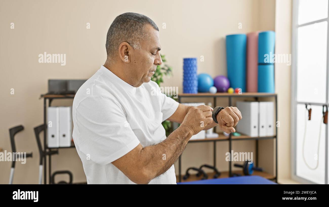 Mature hispanic man checking smartwatch in rehab clinic room with ...