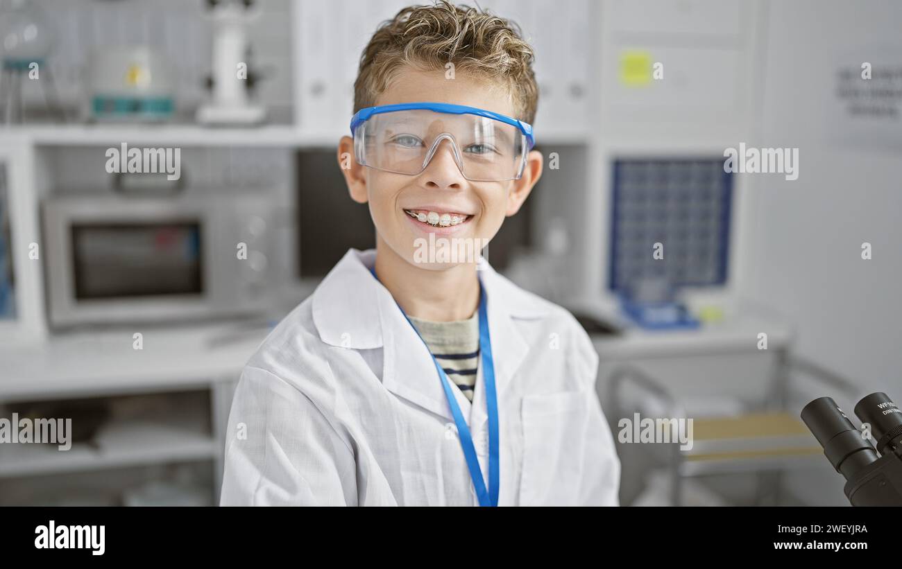 Adorable blond boy scientist, confidently smiling while working on an ...