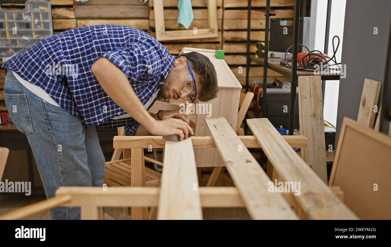 Handsome, serious, young arab man working diligently, sanding wood ...