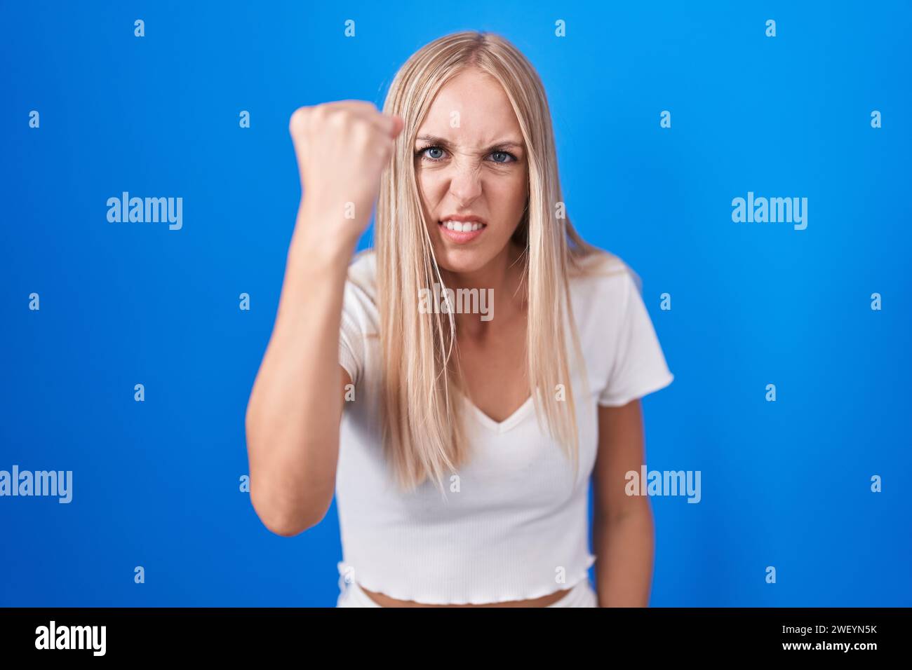 Young caucasian woman standing over blue background angry and mad ...