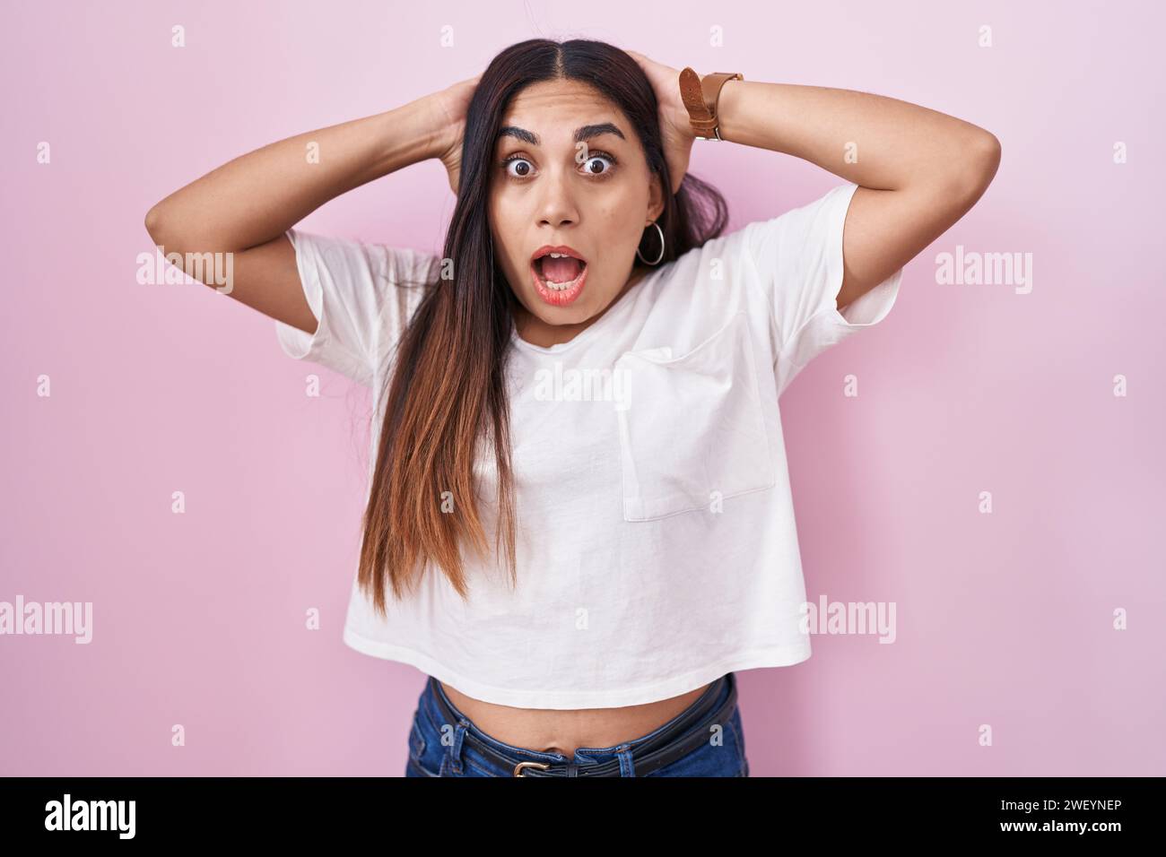 Young arab woman standing over pink background crazy and scared with ...