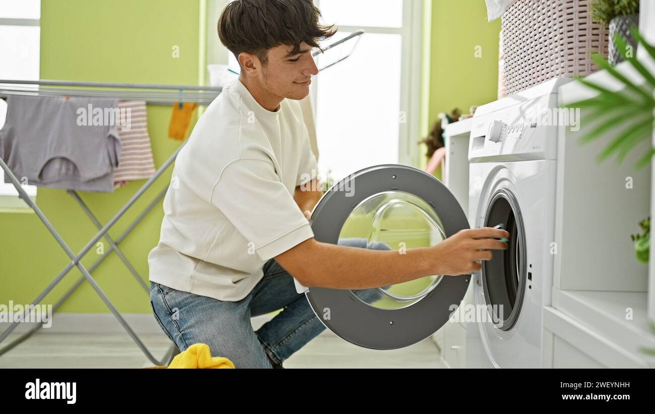 Smiling young hispanic teenager enjoying doing laundry, confidently ...