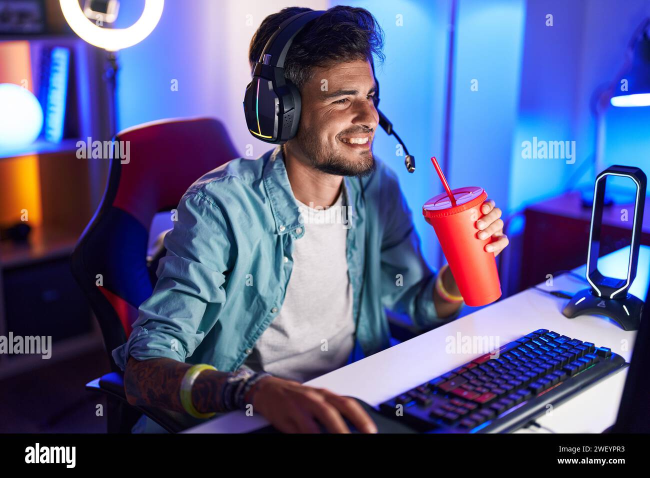 Young hispanic man streamer playing video game drinking beverage at ...