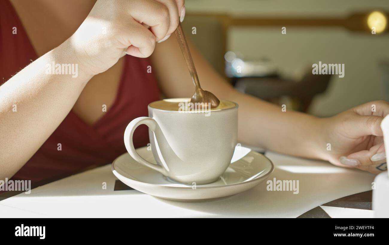 A young adult woman stirs coffee in a bright cafe, showcasing a casual ...