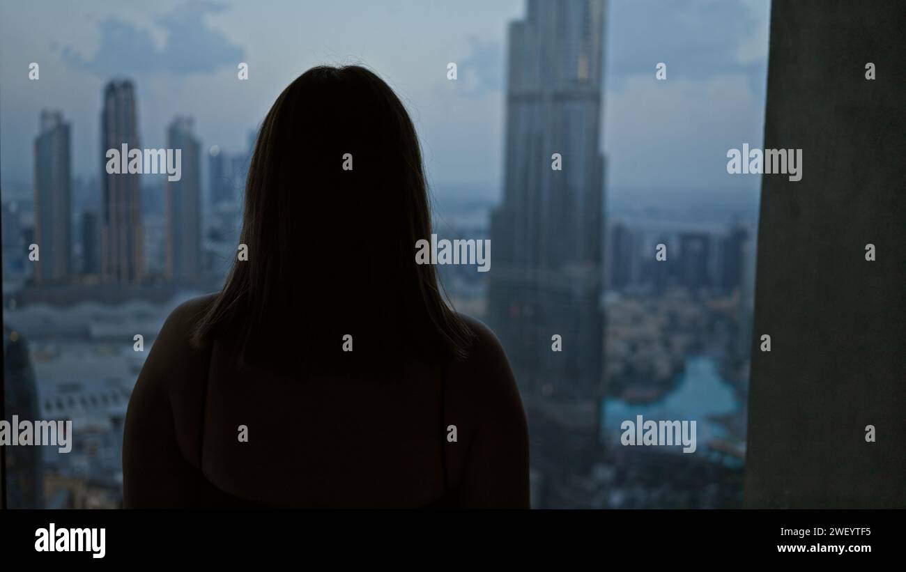 Silhouetted woman observing a blurred cityscape from an observatory ...