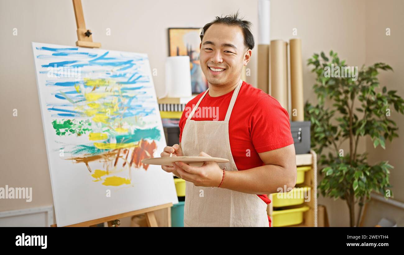 Smiling, confident young chinese man passionately draws in art studio ...