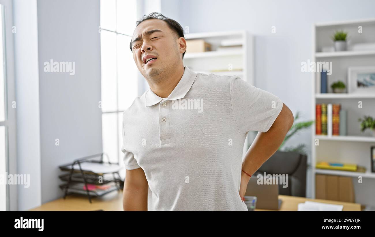 Worried young chinese man worker suffering serious backache, touching ...