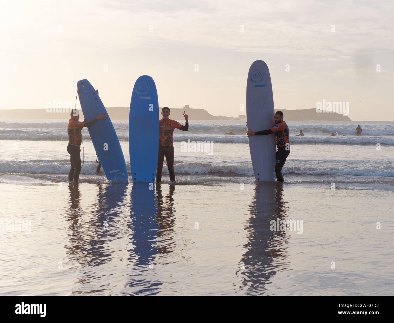 Three male learner surfers smile as they hold their surf boards as the ...