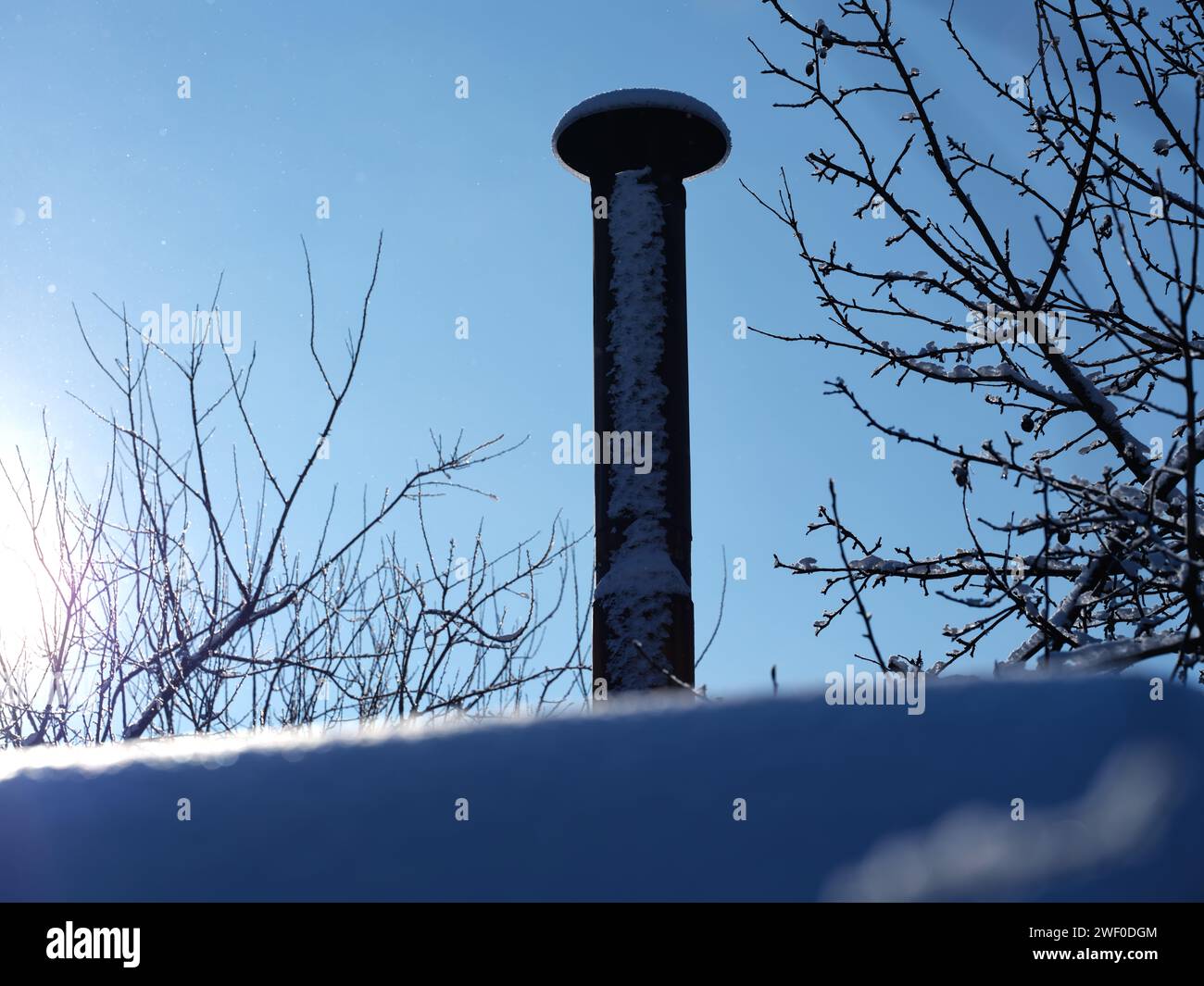 An old metal chimney on a snow-covered roof against blue sky background ...