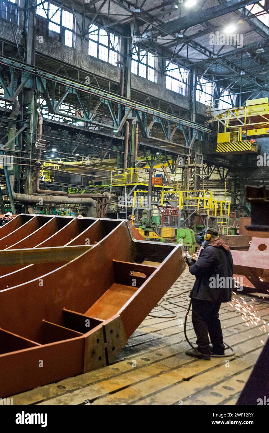 Worker in a mask grinds a metal part at a factory or cuts it with an ...