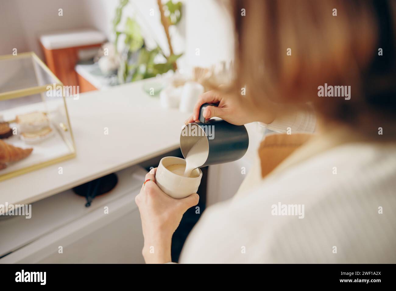 Back view of female barista makes coffee and pours it into a mug while ...