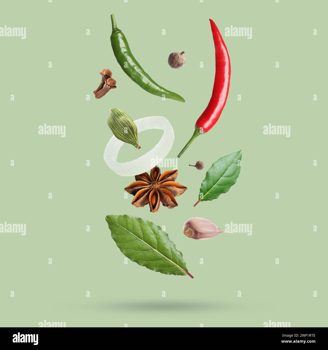 Different spices falling on light green background Stock Photo - Alamy