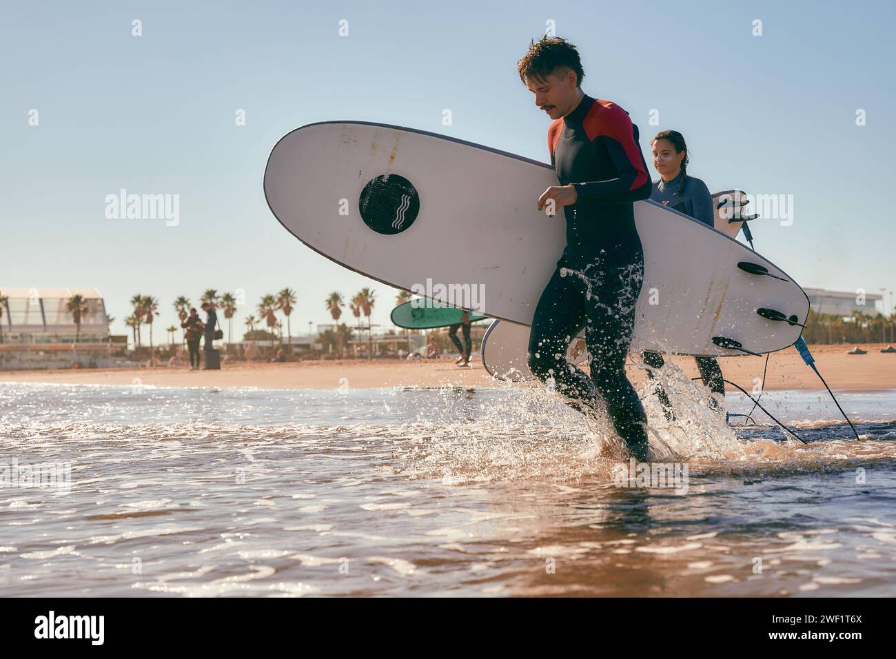 Side view of surfers in wetsuits running into the sea holding ...
