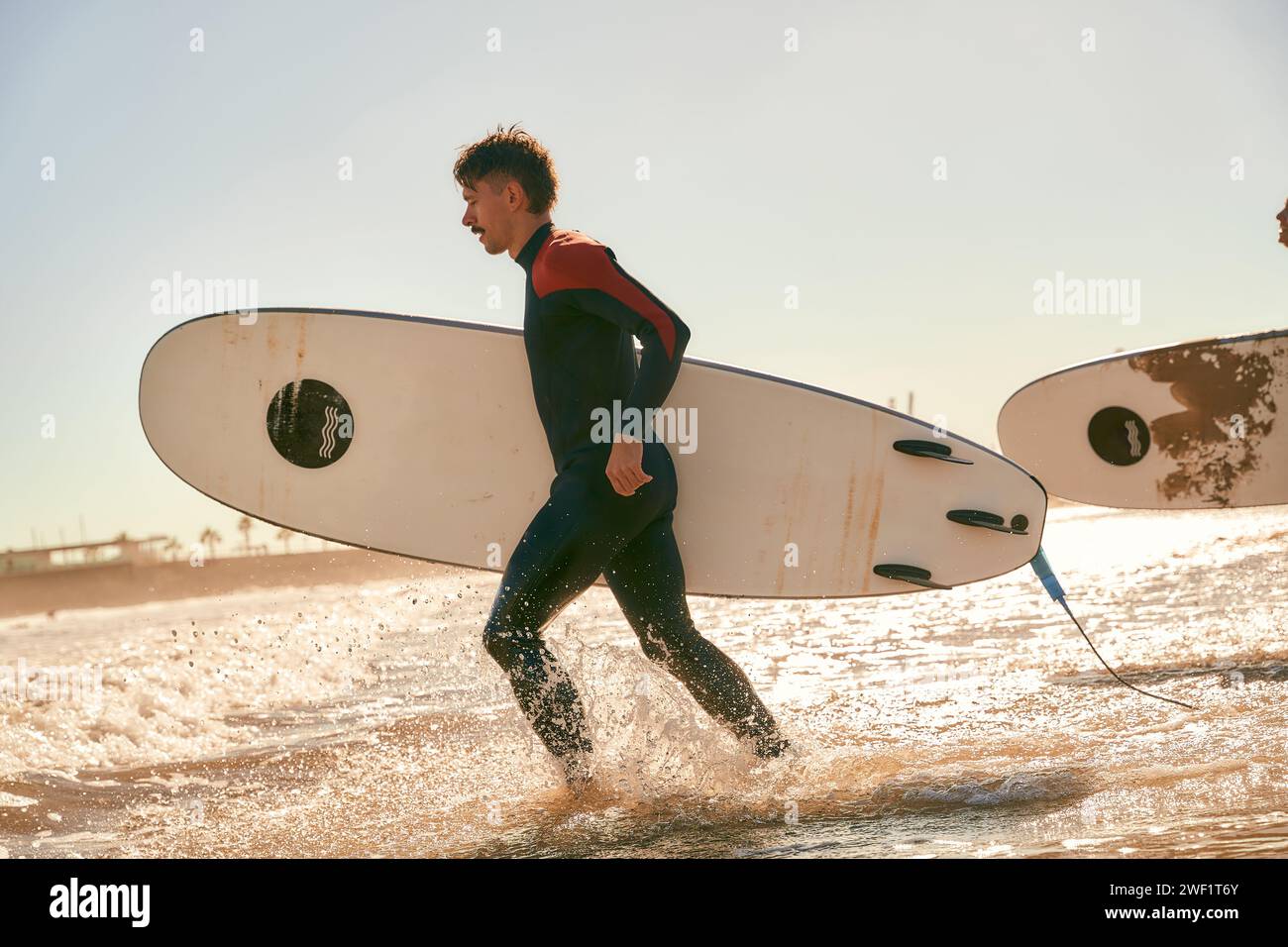 Group of happy surfers in wetsuits running into the sea holding ...