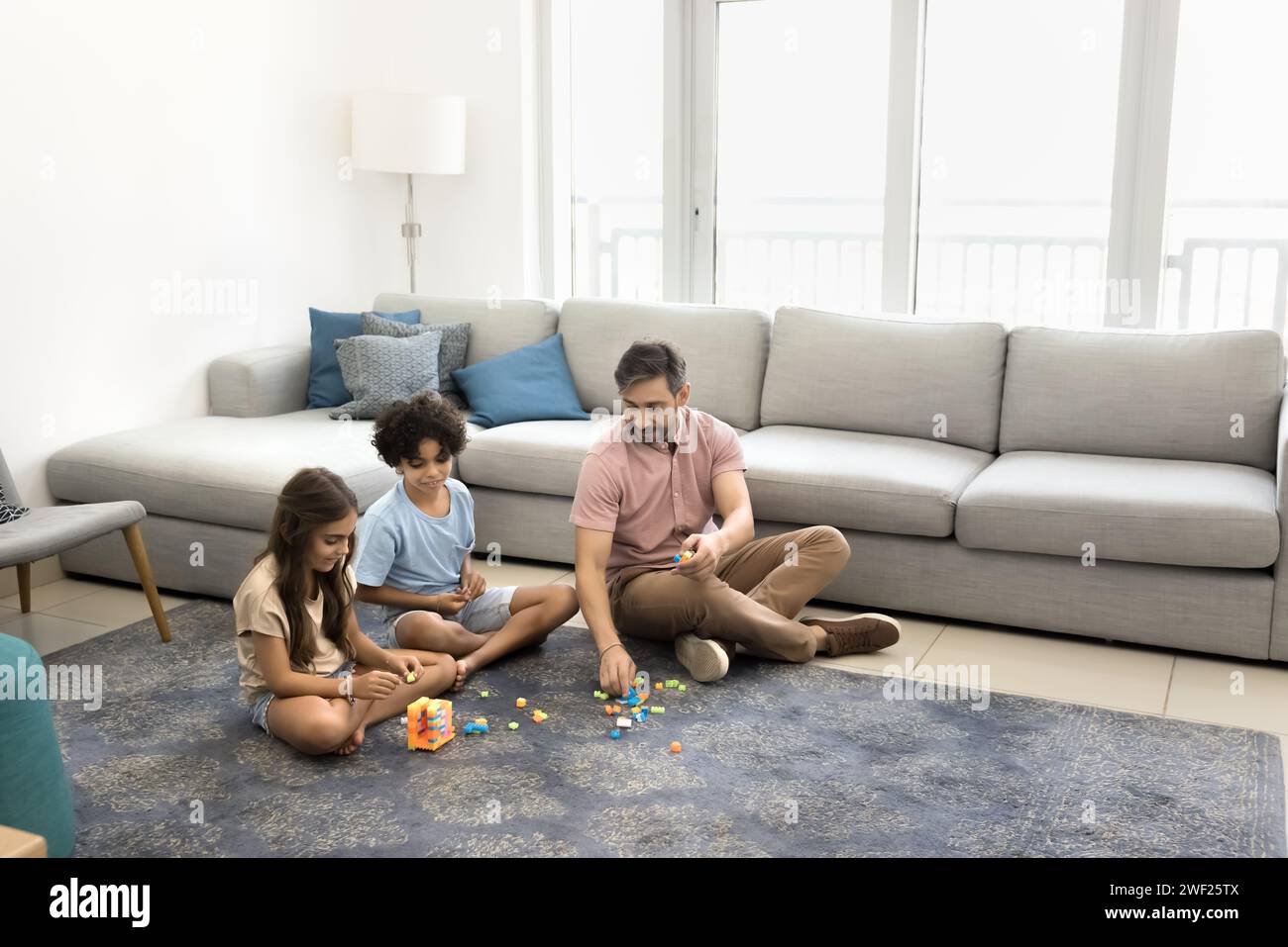 Engaged dad helping sibling kids to construct tower Stock Photo - Alamy