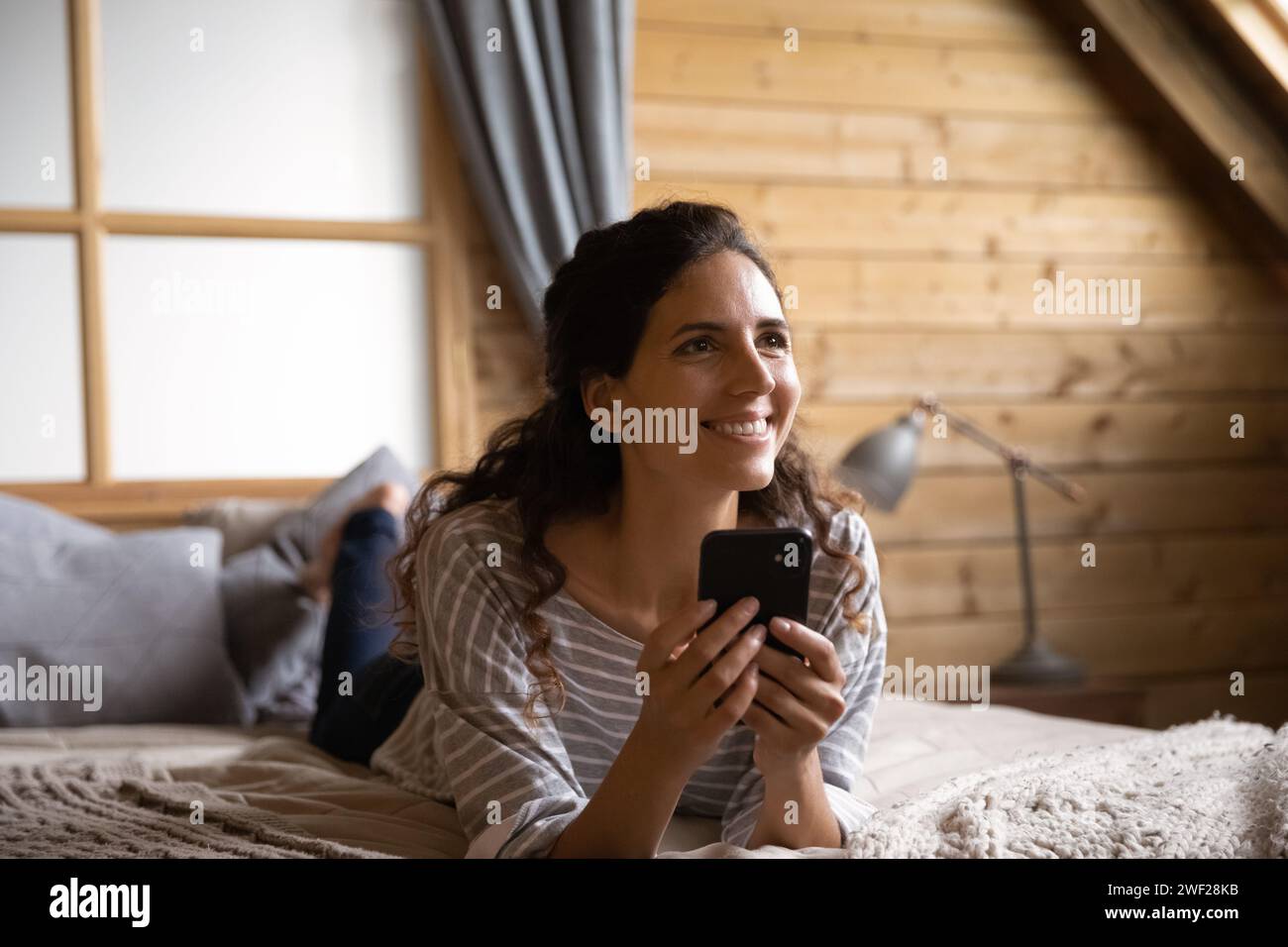 Dreamy young hispanic female lie on bed relax with smartphone Stock ...
