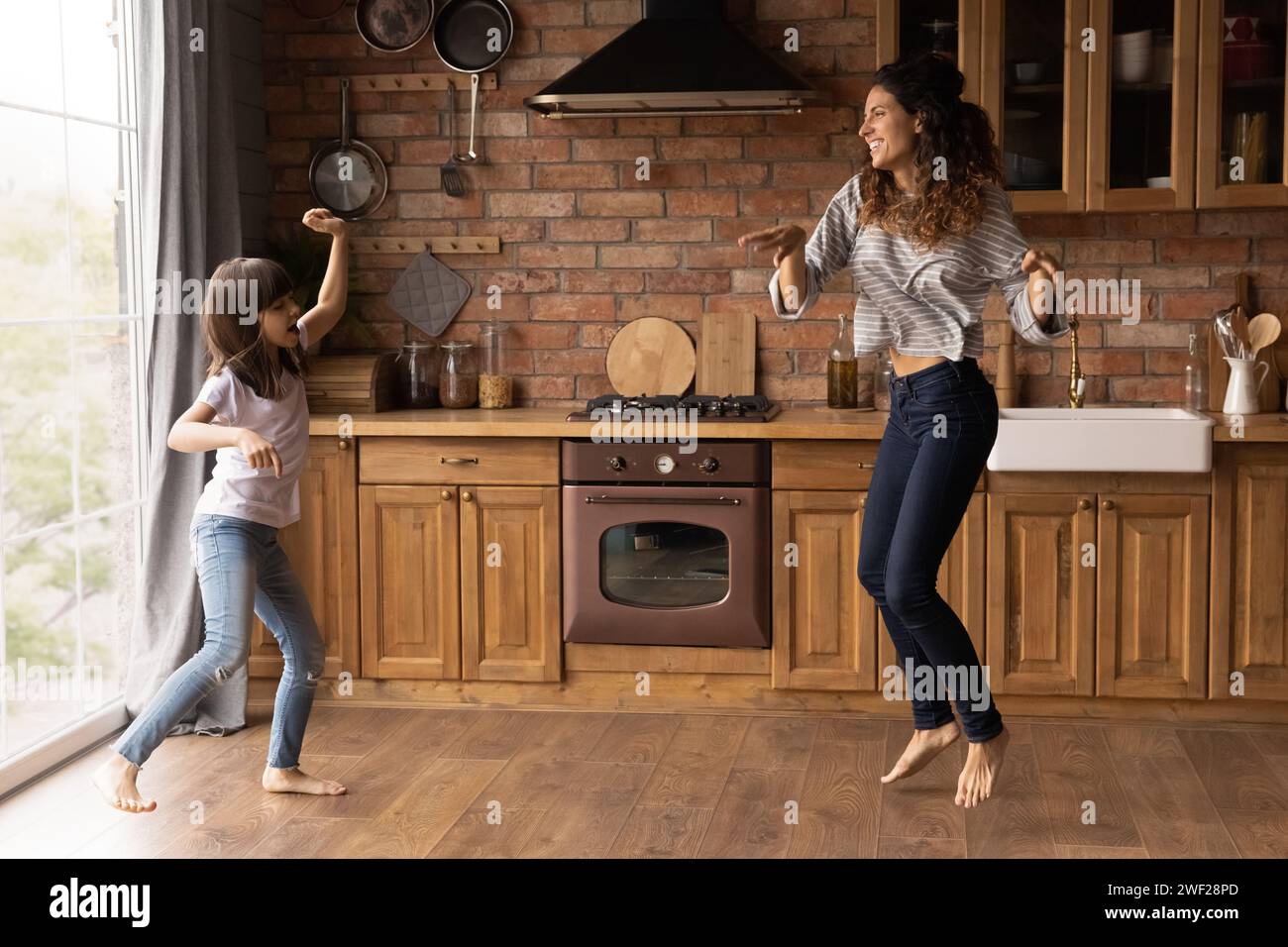 Joyful latin mother preteen daughter dance jump at modern kitchen Stock ...