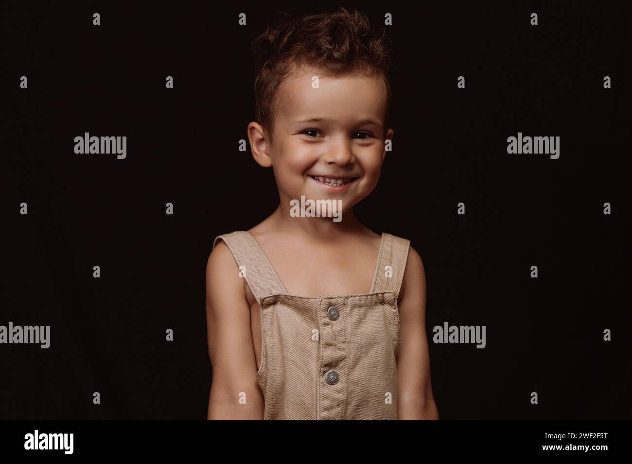 beautiful happy boy in overalls with a stylish hairstyle smiles on a ...