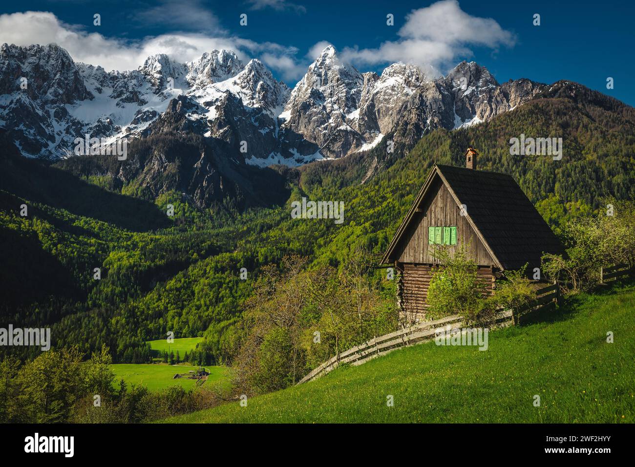 Majestic spring alpine scenery with cozy wooden hut on the green meadow ...