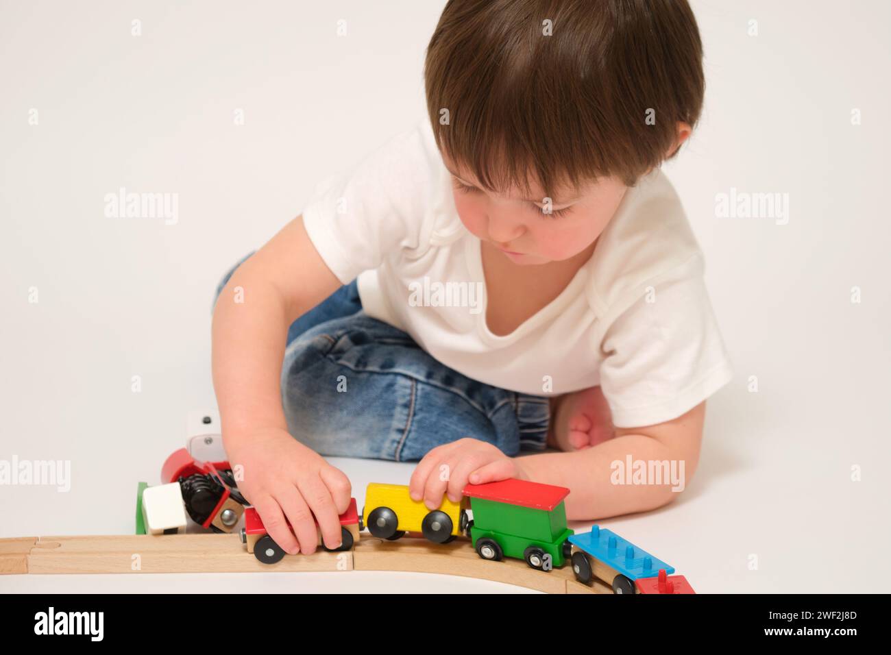 Toddler baby is playing train cars on the railroad, studio white ...