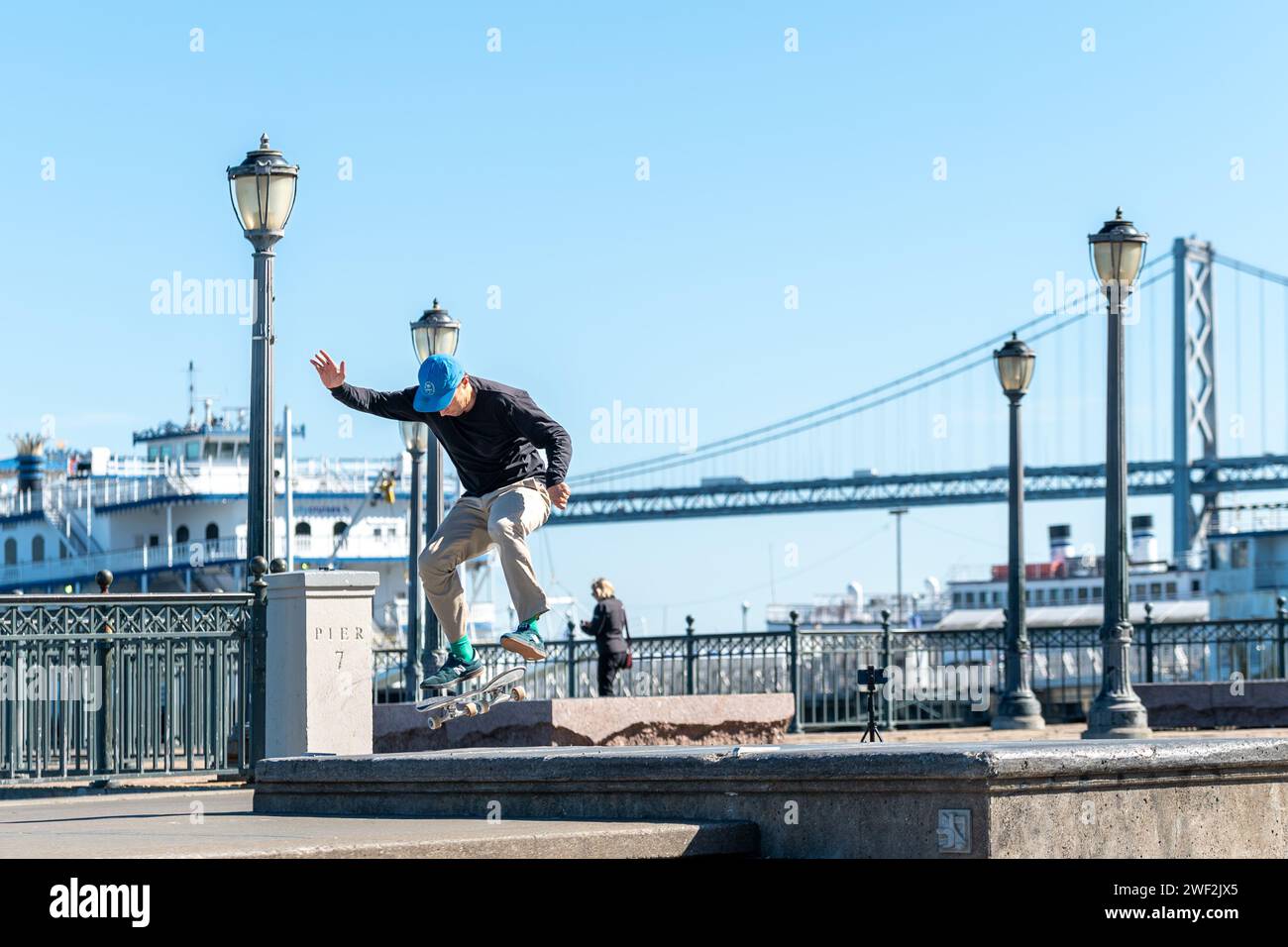 Skateboarder executing trick on concrete step with suspension bridge ...
