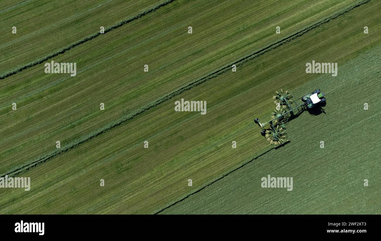 Farmer cutting grass to straight rows with tractor and large roundabout ...