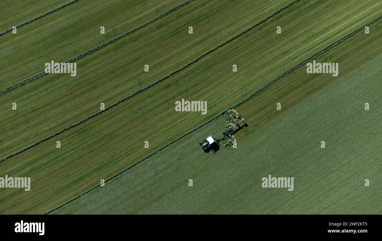 Farmer cutting grass to straight rows with tractor and large roundabout ...