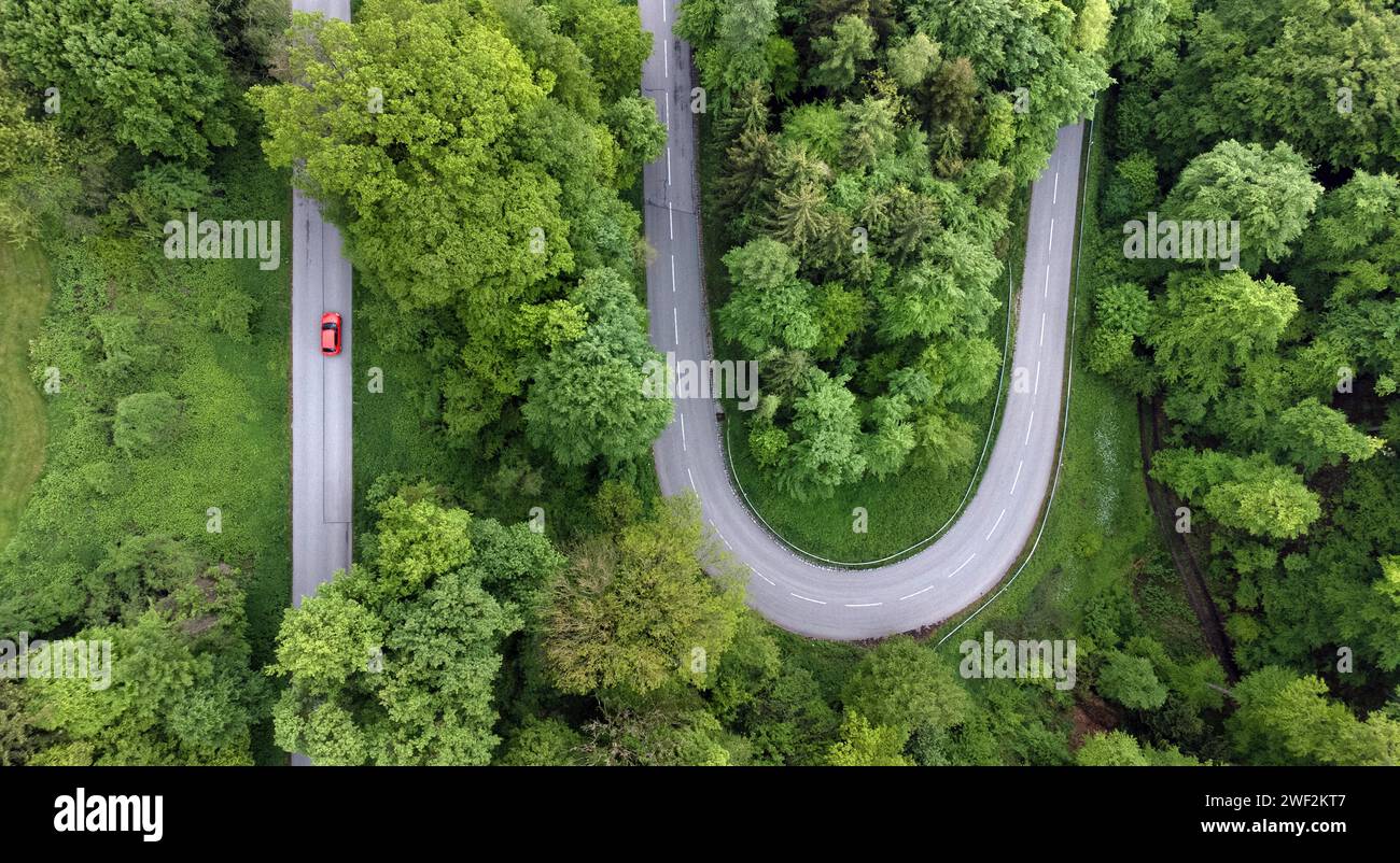Red car driving on serpentine road through green landscape, drone shot ...