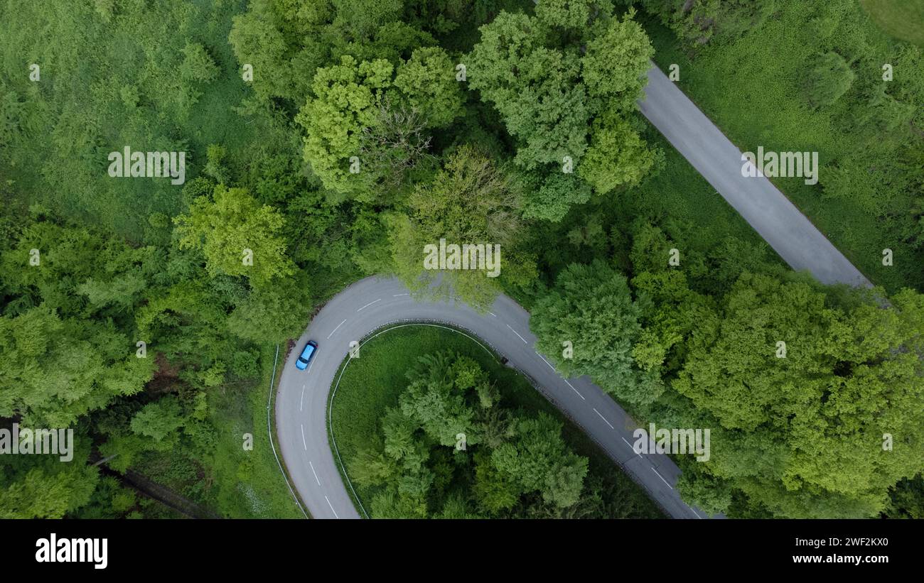 Blue car driving on serpentine road through green landscape, drone shot ...