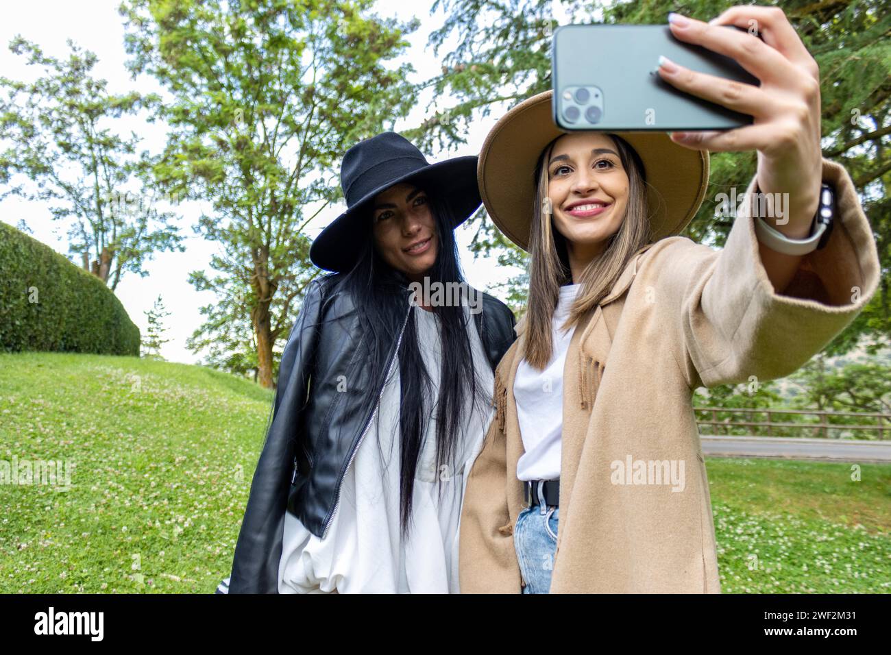 Front view of two stylish friends with hats standing and taking a selfie at the park Stock Photo ...