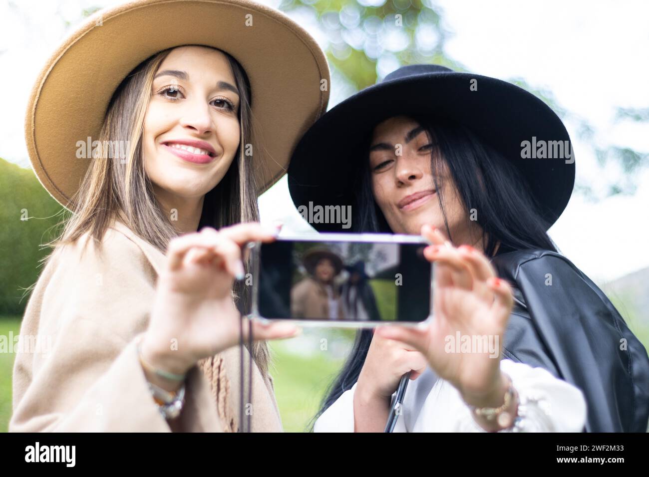 Front view of two stylish friends both grabbing a cell phones to take a ...