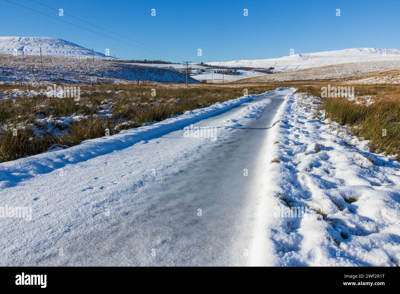 A frozen pathway or road in the Yorkshire Dales in winter, with lots of snow on the ground and ...