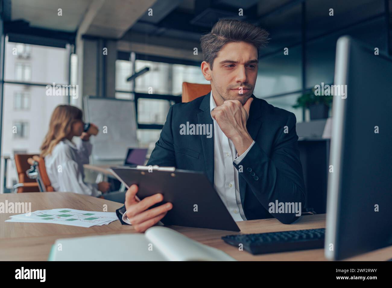 Male manager sitting at desk with clipboard and thinking about project ...