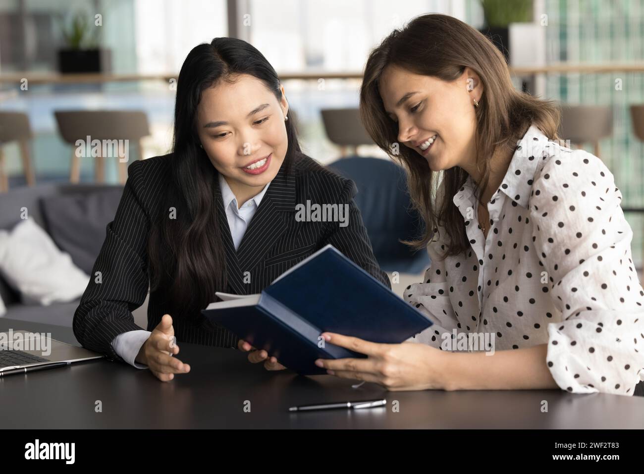 Two cheerful multiethnic female colleagues talking at workplace Stock ...