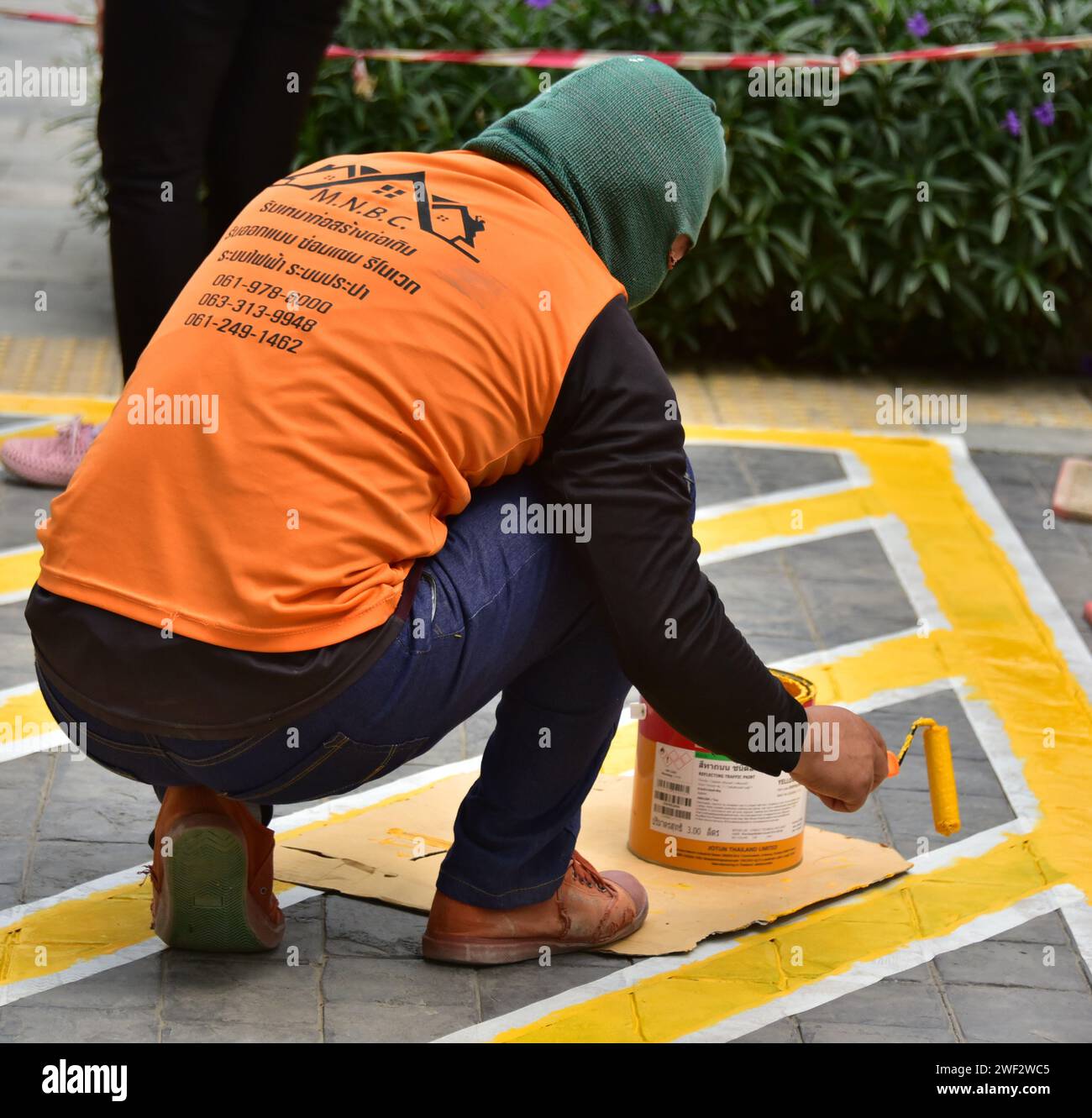 A person uses a small roller brush to paint yellow warning lines on a ...