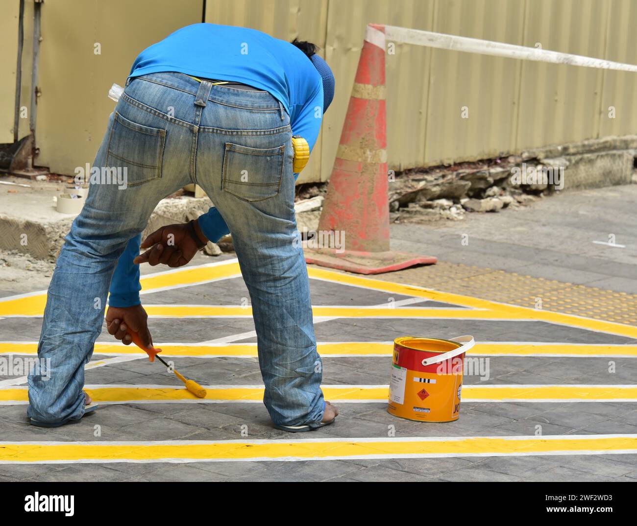 A person uses a small roller brush to paint yellow warning lines on a ...