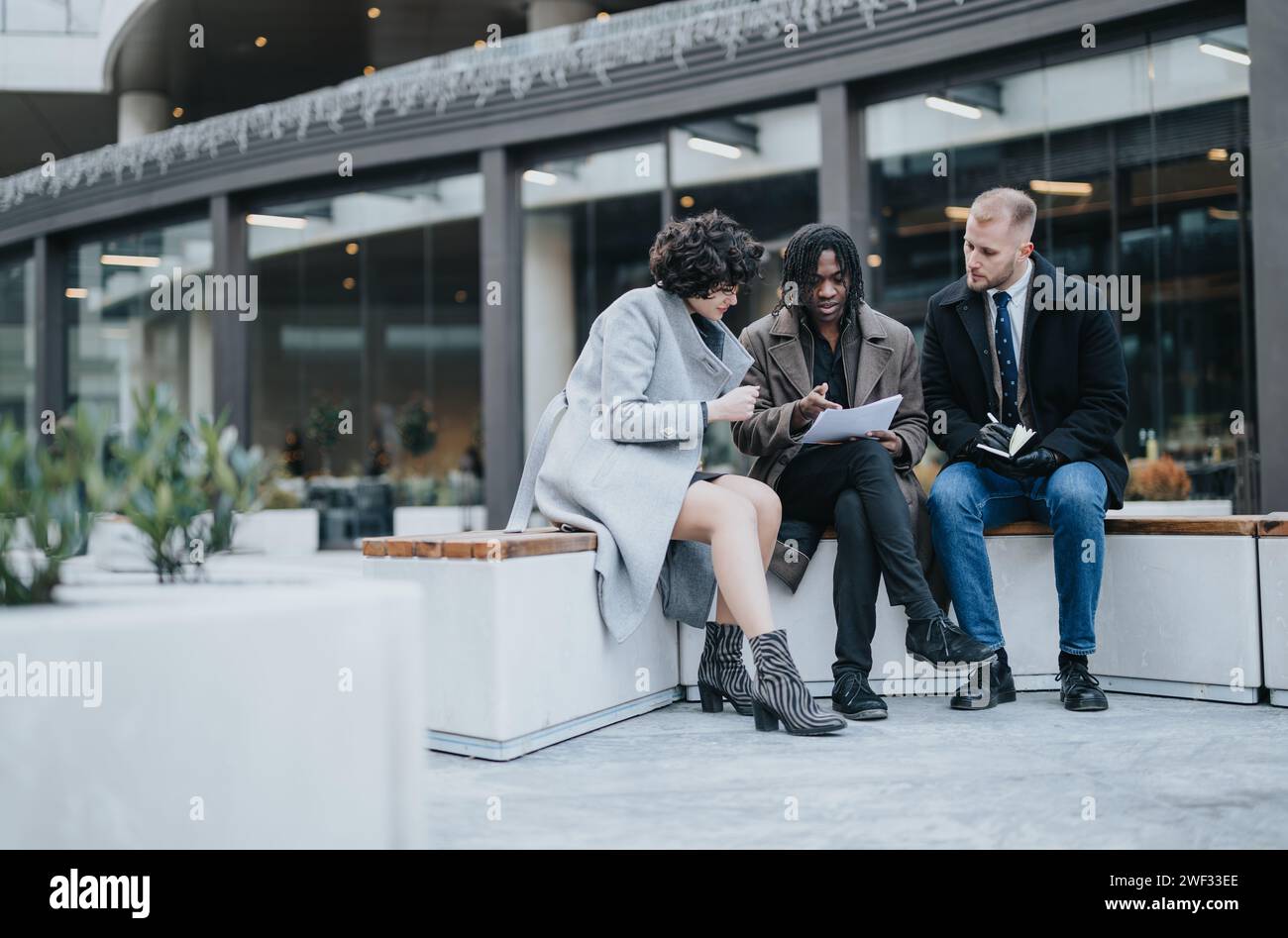 Three colleagues discussing work-related matters on a bench outside a ...