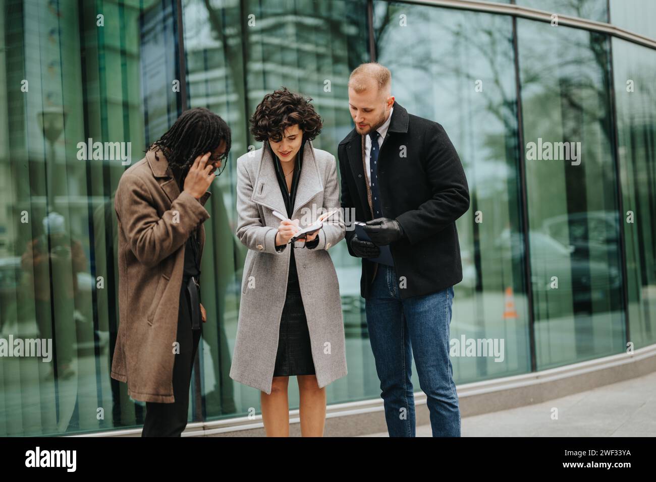 Three people discussing work on a smart phone outside modern office ...