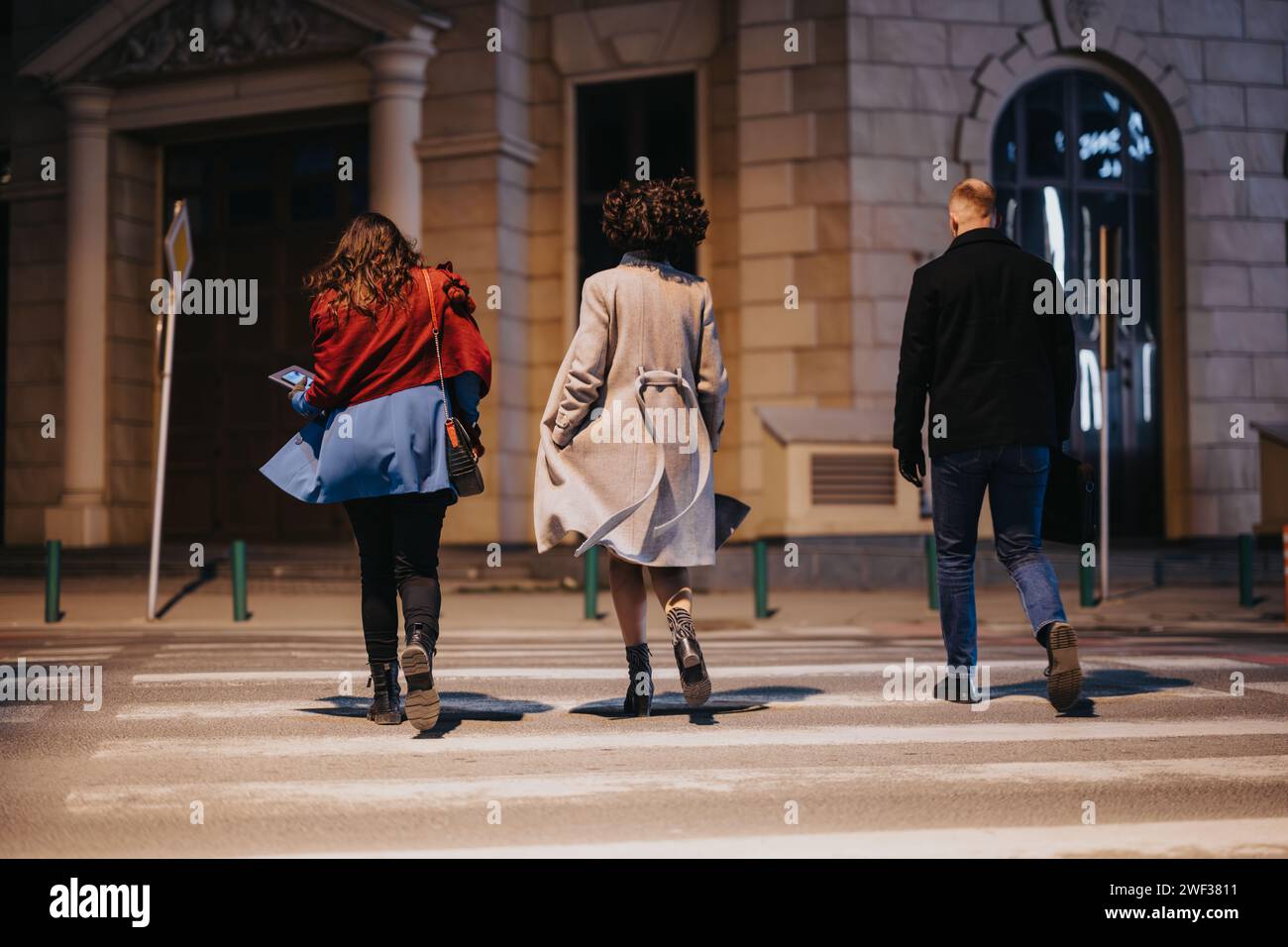 Three friends captured from behind, crossing the street at night in a ...