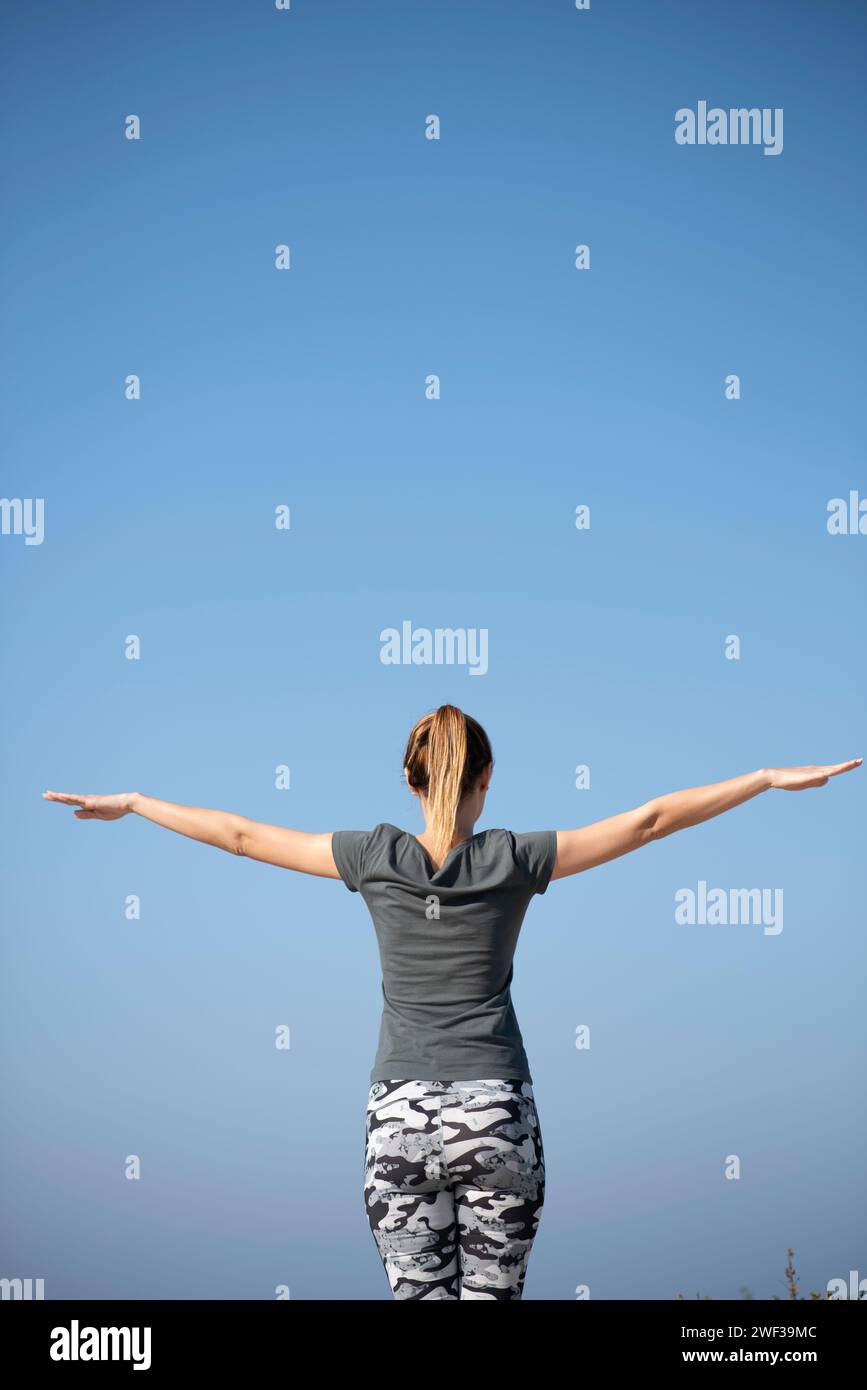 Rear view of young woman arms outstretched against blue sky Stock Photo ...