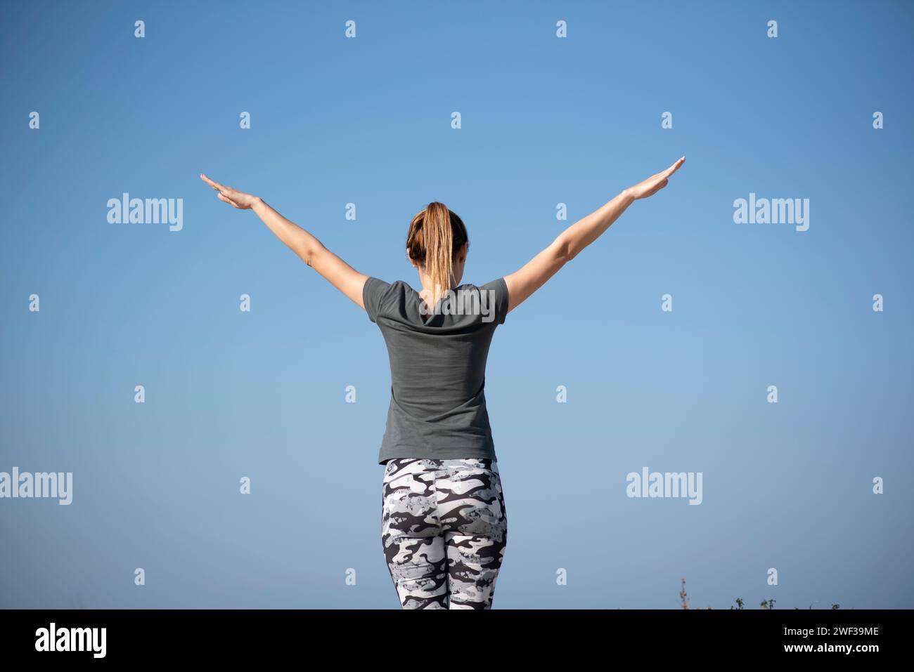 Rear view of young woman arms outstretched against blue sky Stock Photo ...