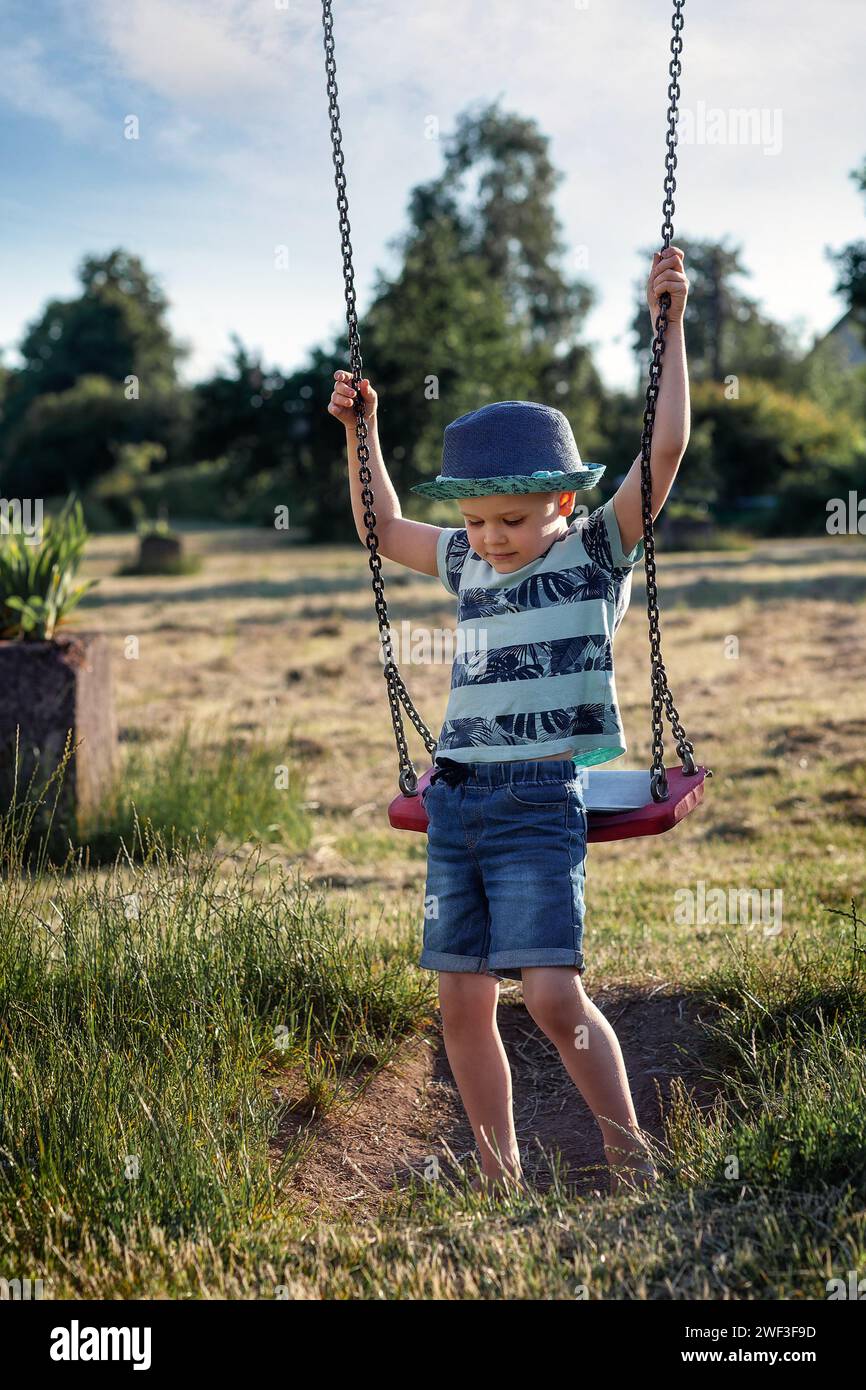A little boy in a blue hat is trying to reach and climb the outdoor ...