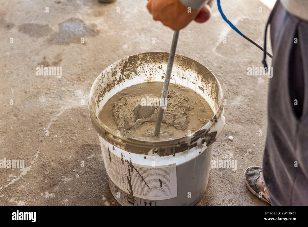 The worker mixes the solution in a bucket using a mixer. Mixing plaster ...