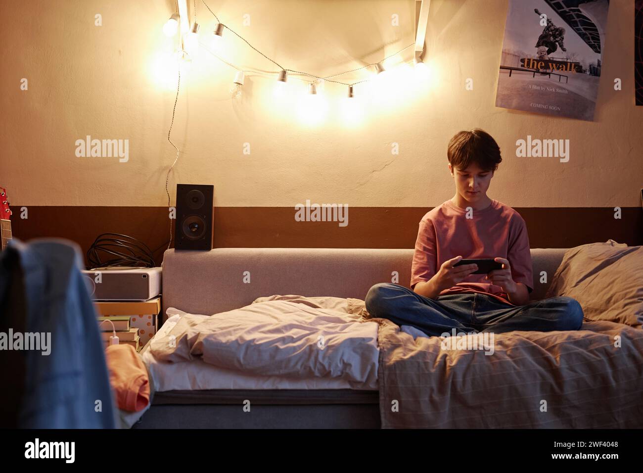 Wide angle portrait of teen boy playing mobile games sitting on bed ...