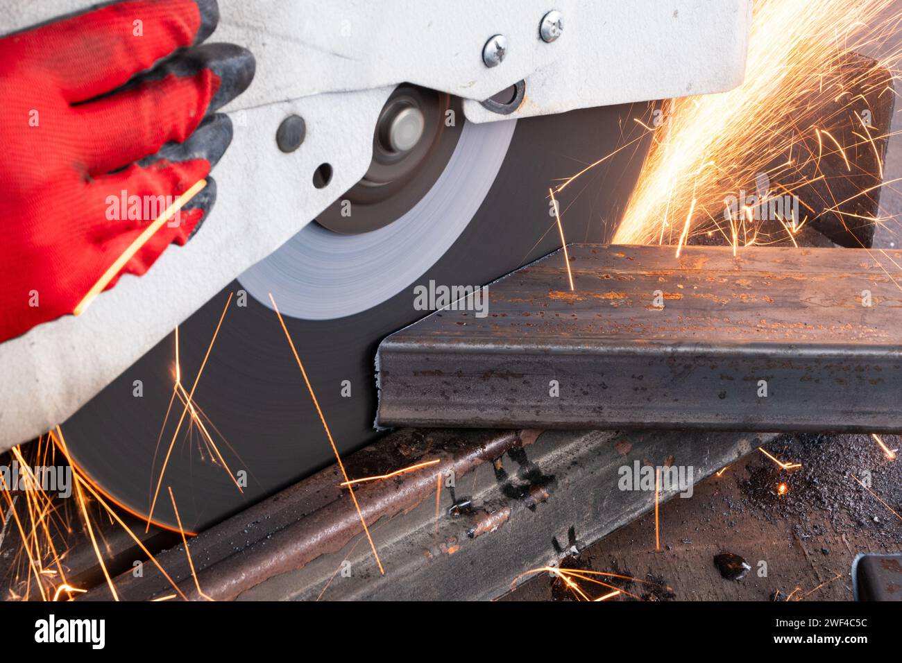 Metal worker cutting a rectangular steel tube using a circular saw, creating sparks, showcasing ...